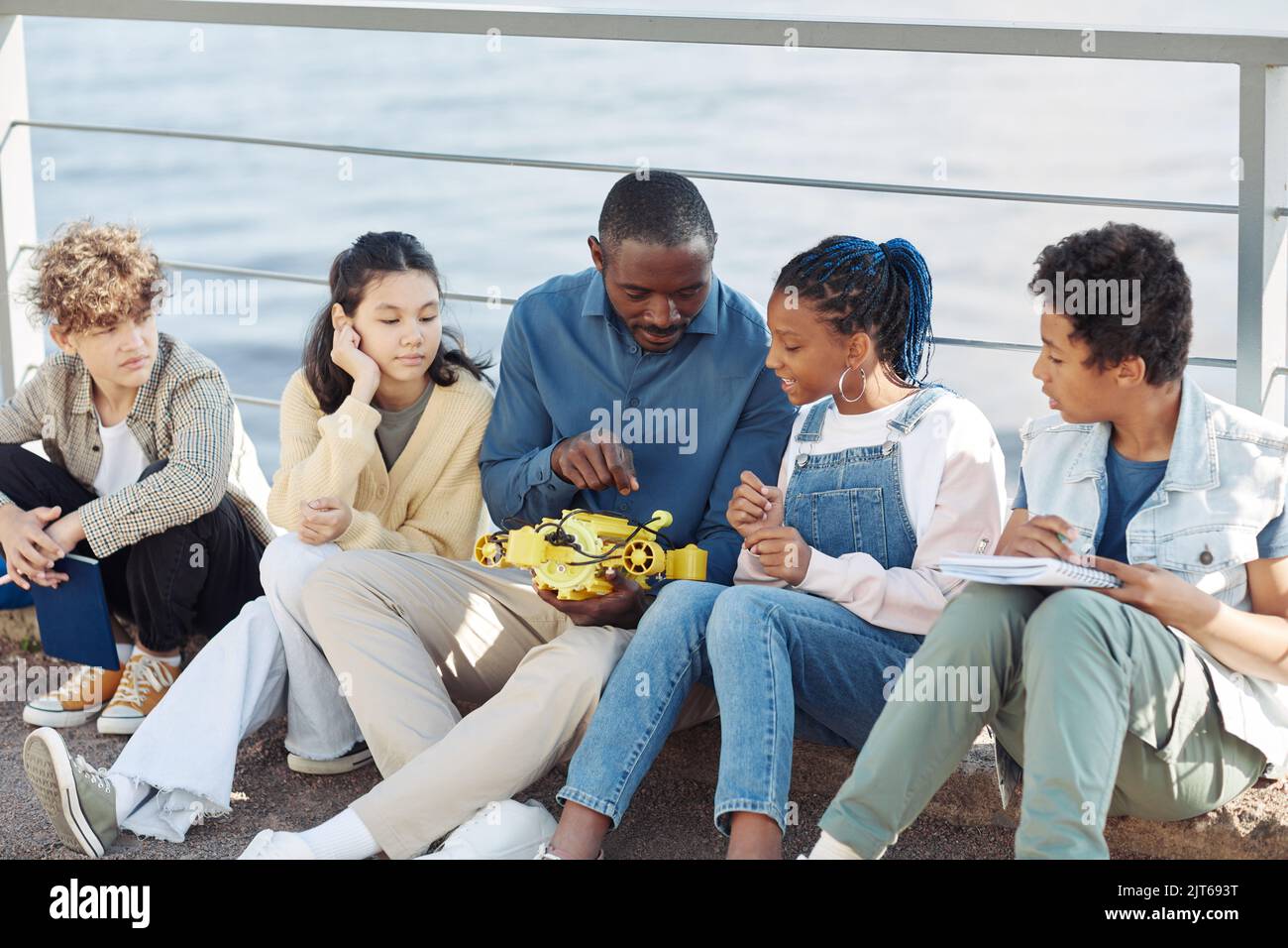 Portrait of black male teacher showing robot model to kids outdoors ...