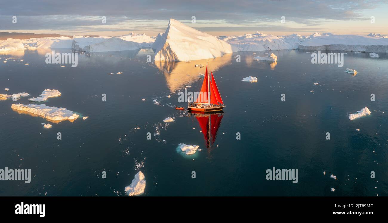 A small boat among icebergs. Sailboat cruising among floating icebergs ...