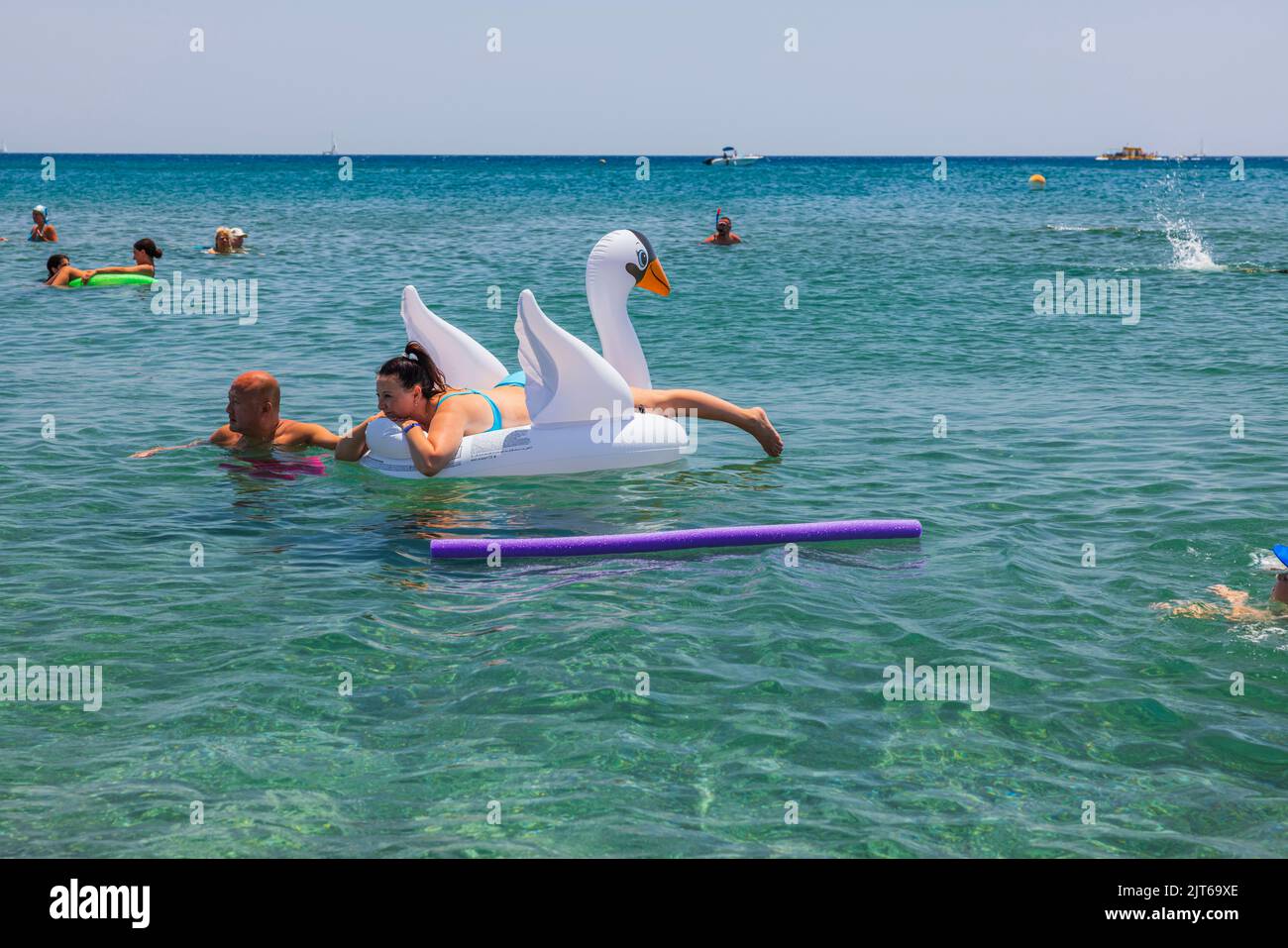 View of people swimming in sea. Couple on inflatable white swan on ...