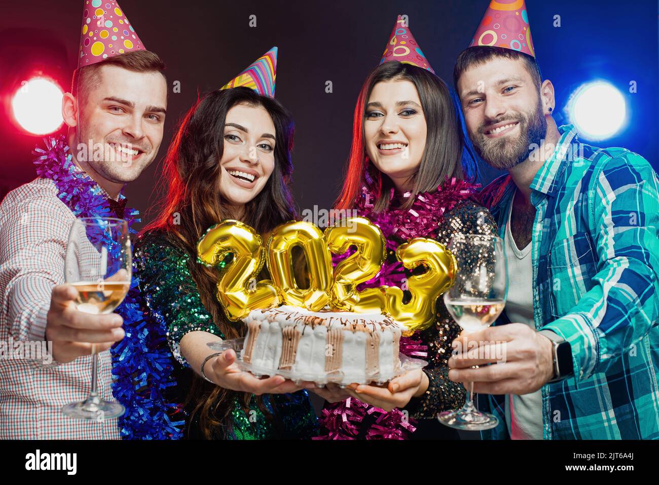 Young adult students in tinsel and party hats hold 2023 number cake at ...