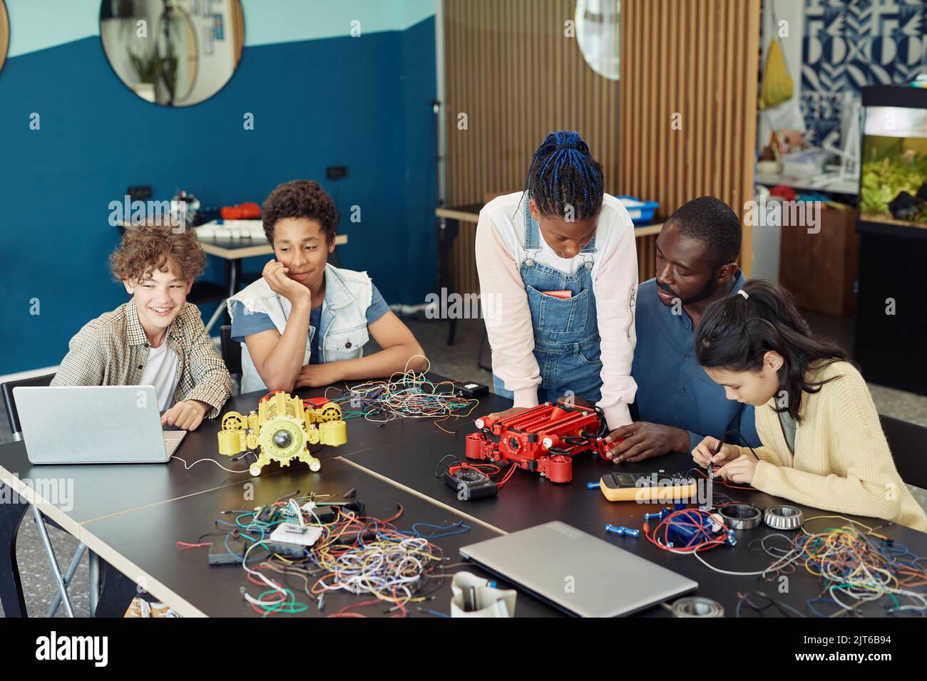 Diverse group of kids with male teacher building robots together during ...