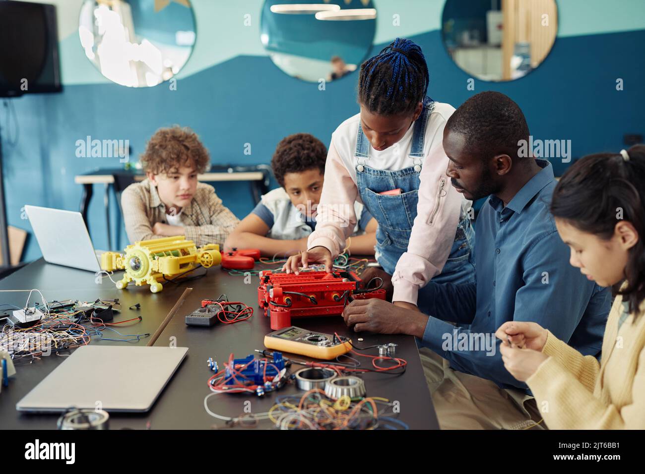 Portrait of black teenage girl building robot with diverse group of ...