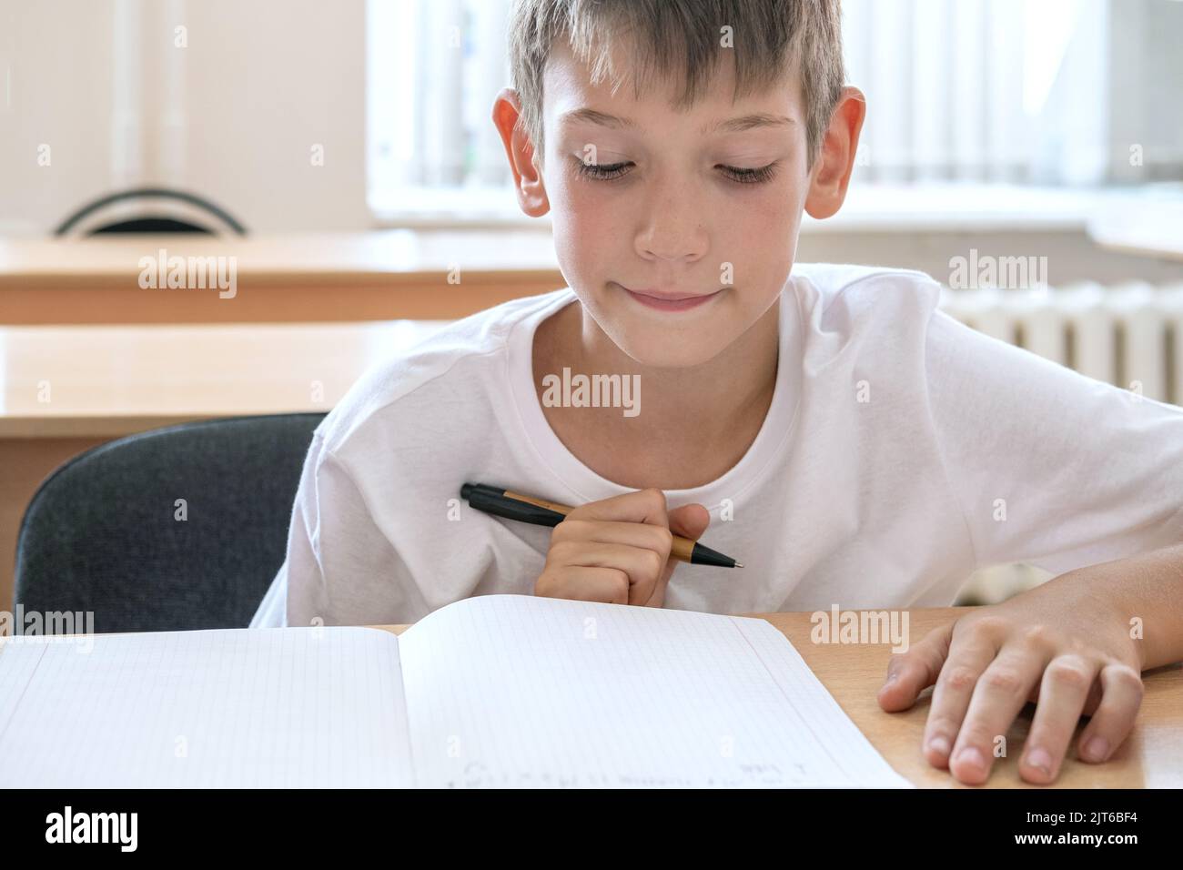 A focused boy doing homework, writing text in a notebook at the table ...