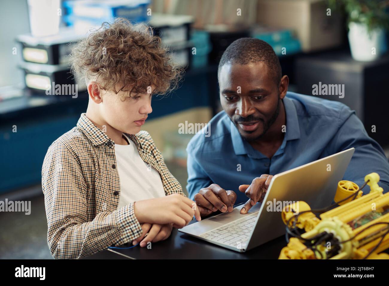 Portrait of black male teacher helping young boy building robot during ...