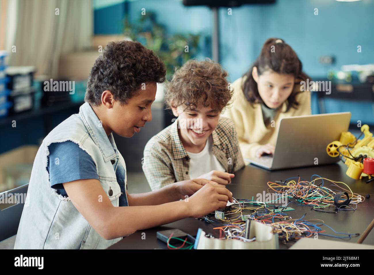 Portrait of two smiling teenage boys building robot together during ...