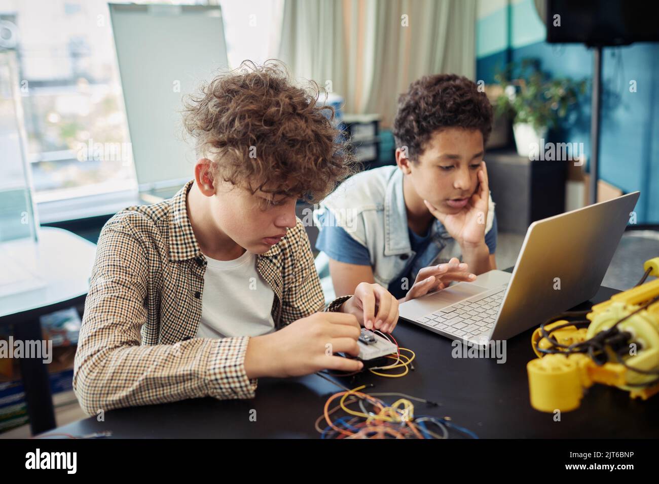 Portrait of two boys using laptop together and programming robots during engineering class at ...