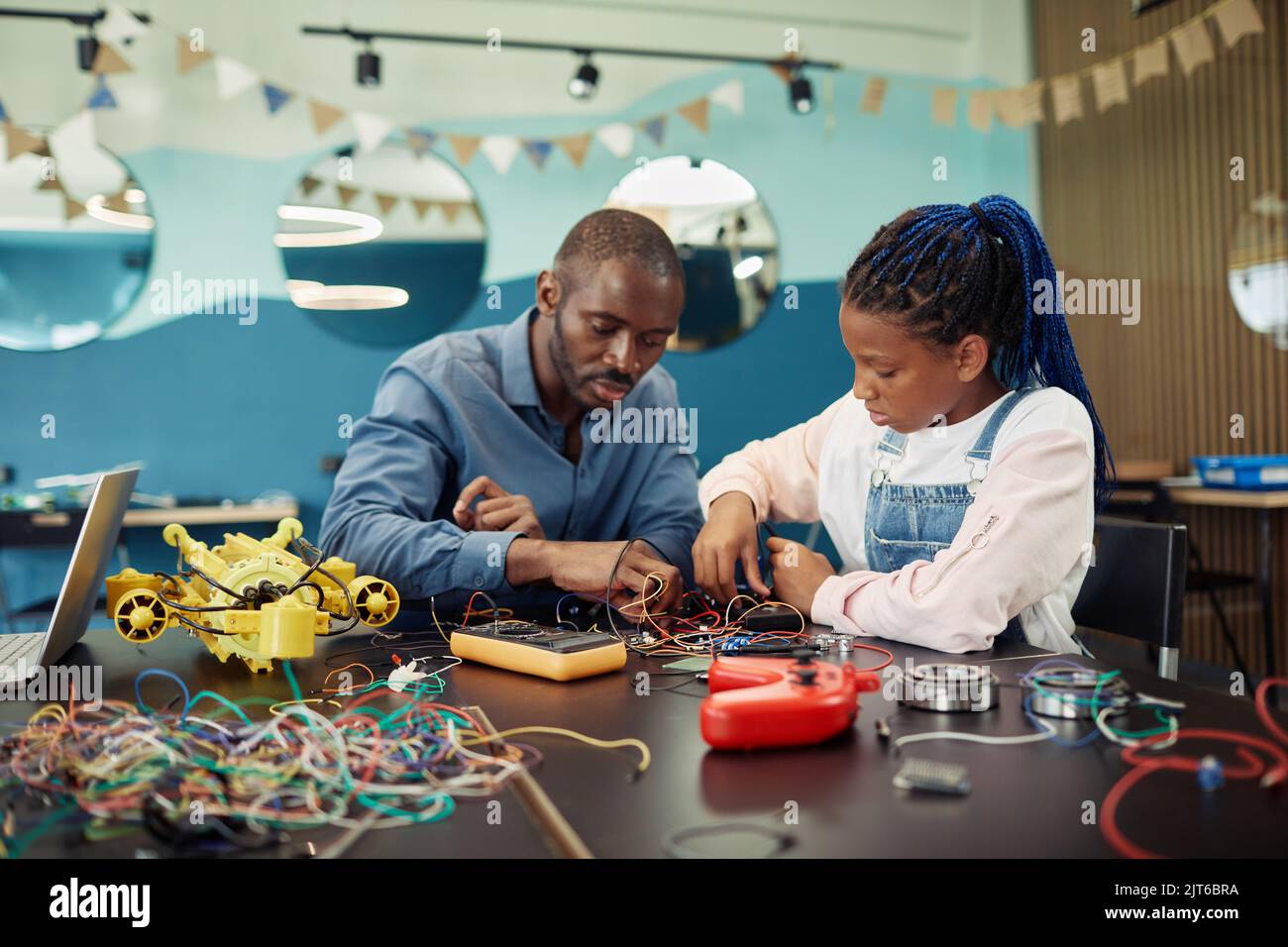 Portrait of black young girl building robots with male teacher helping ...