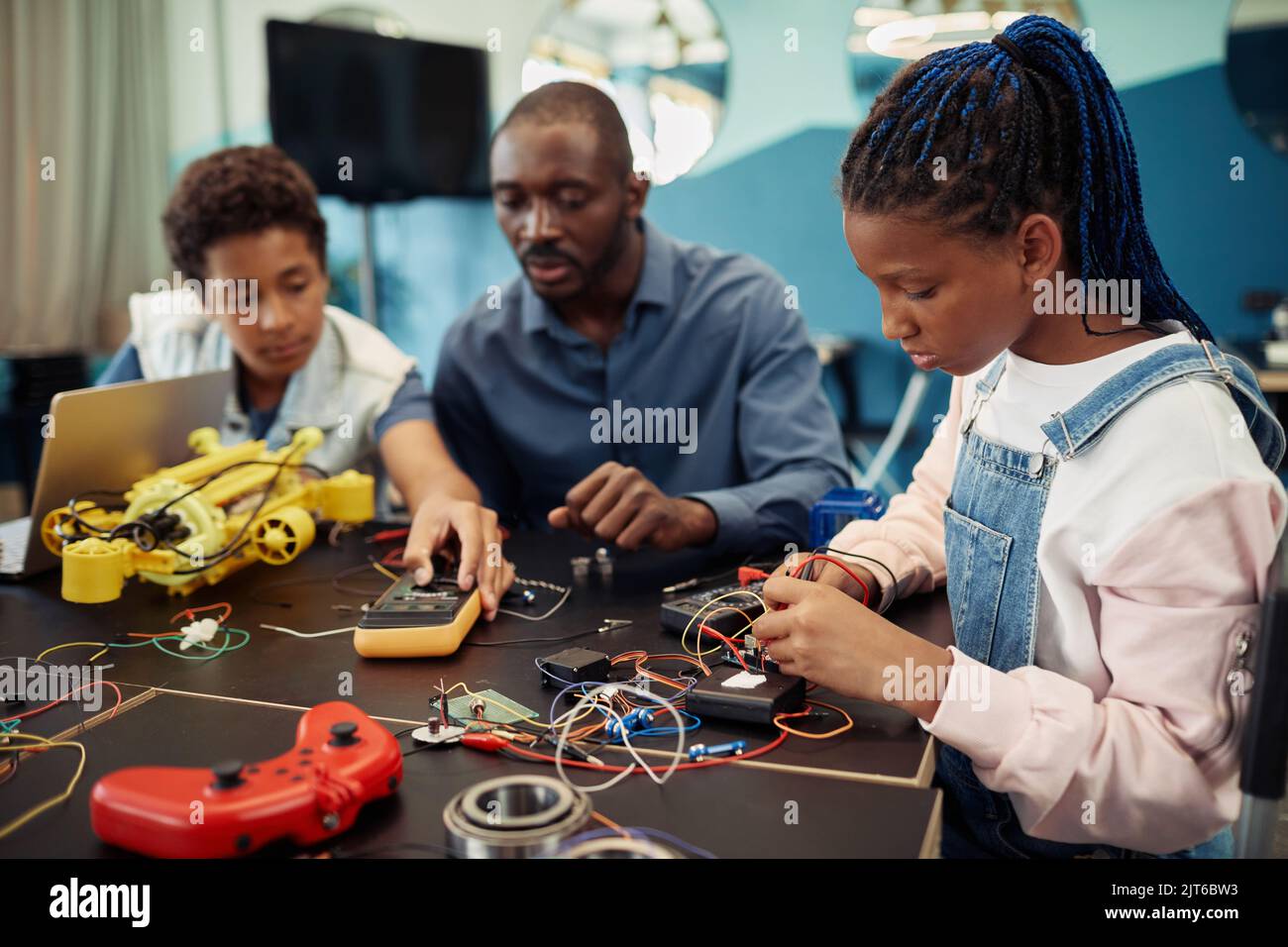 Side view portrait of young black girl building robots with male ...