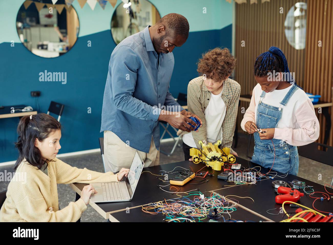 Portrait of male teacher helping children building robots in ...