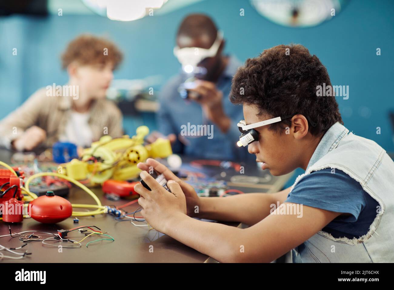Side view portrait of young black boy building robots in engineering ...