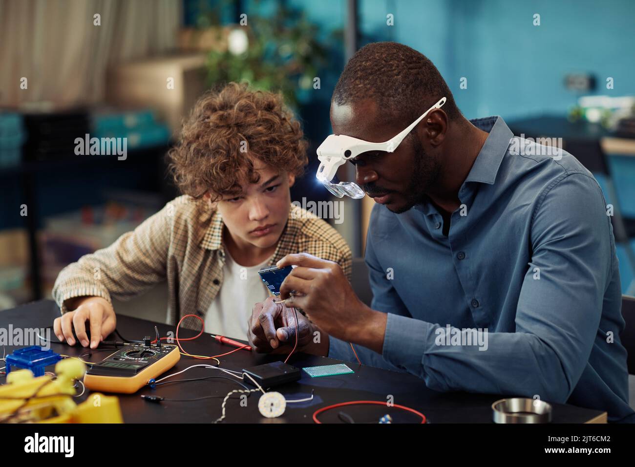 Portrait of young teenage boy building robots in engineering class with male teacher helping ...