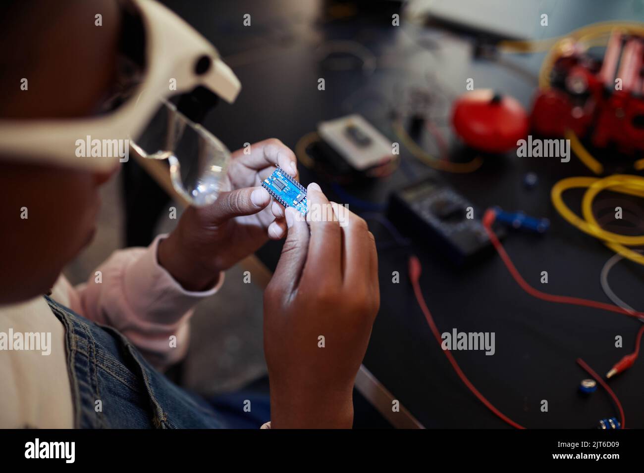 Close up of black young boy holding circuit chip while building robot ...
