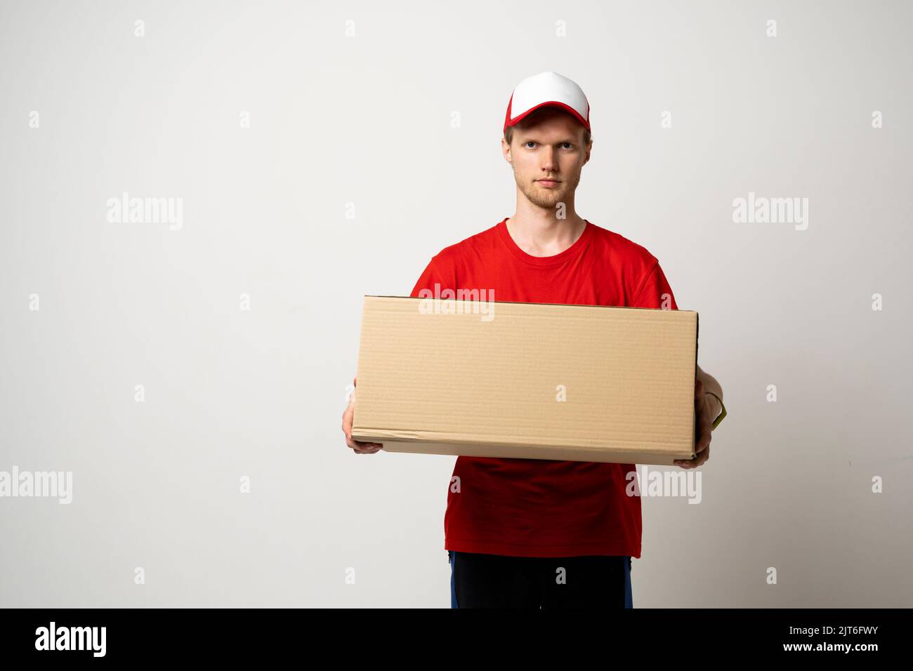 Young delivery man, courier in a red uniform with a big parcel in a ...