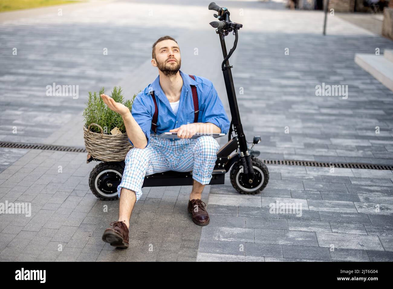 Portrait of stylish weird man sit with laptop on electric scooter ...