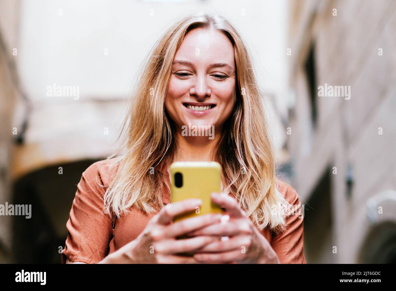 attractive young blonde woman smiling while using her smart phone in ...