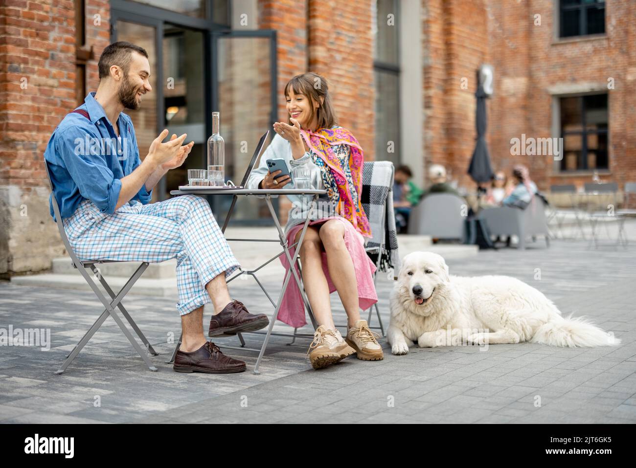 Stylish couple of colleagues have a conversation, sitting with dog in ...