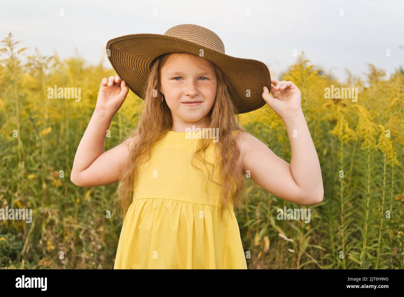 Happy and smiling cute little girl in yellow dress and hat walks in a ...