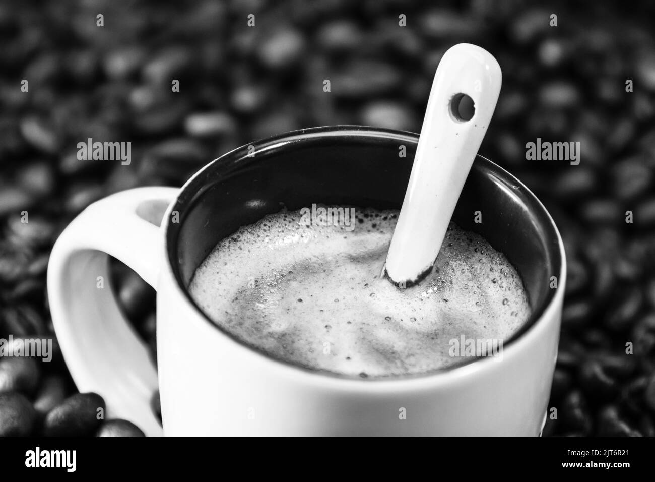 A grayscale closeup of a mug with hot expresso on roasted coffee beans ...