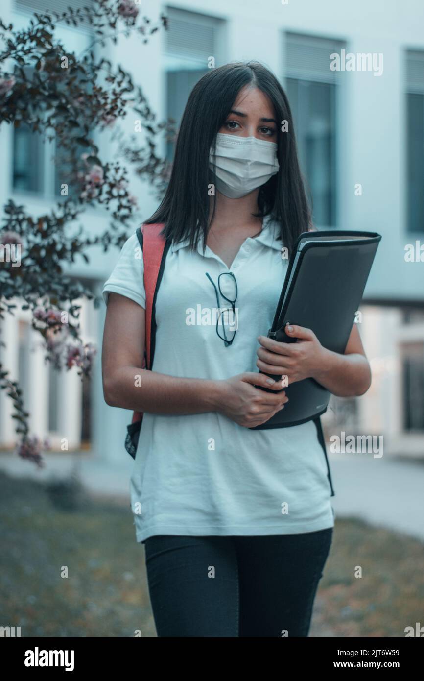 A Caucasian woman with a white mask on her face walking with documents ...