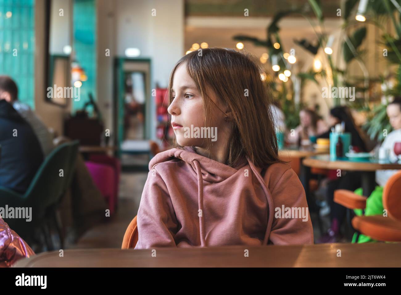 a cute brooding girl sits at a table in a cafe and looks out the window ...