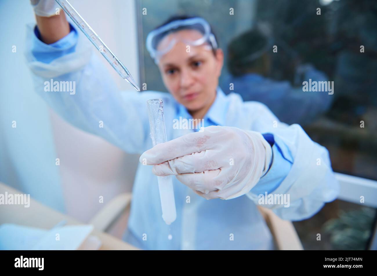 Focus on test tube and graduated lab pipette in a blurred woman ...