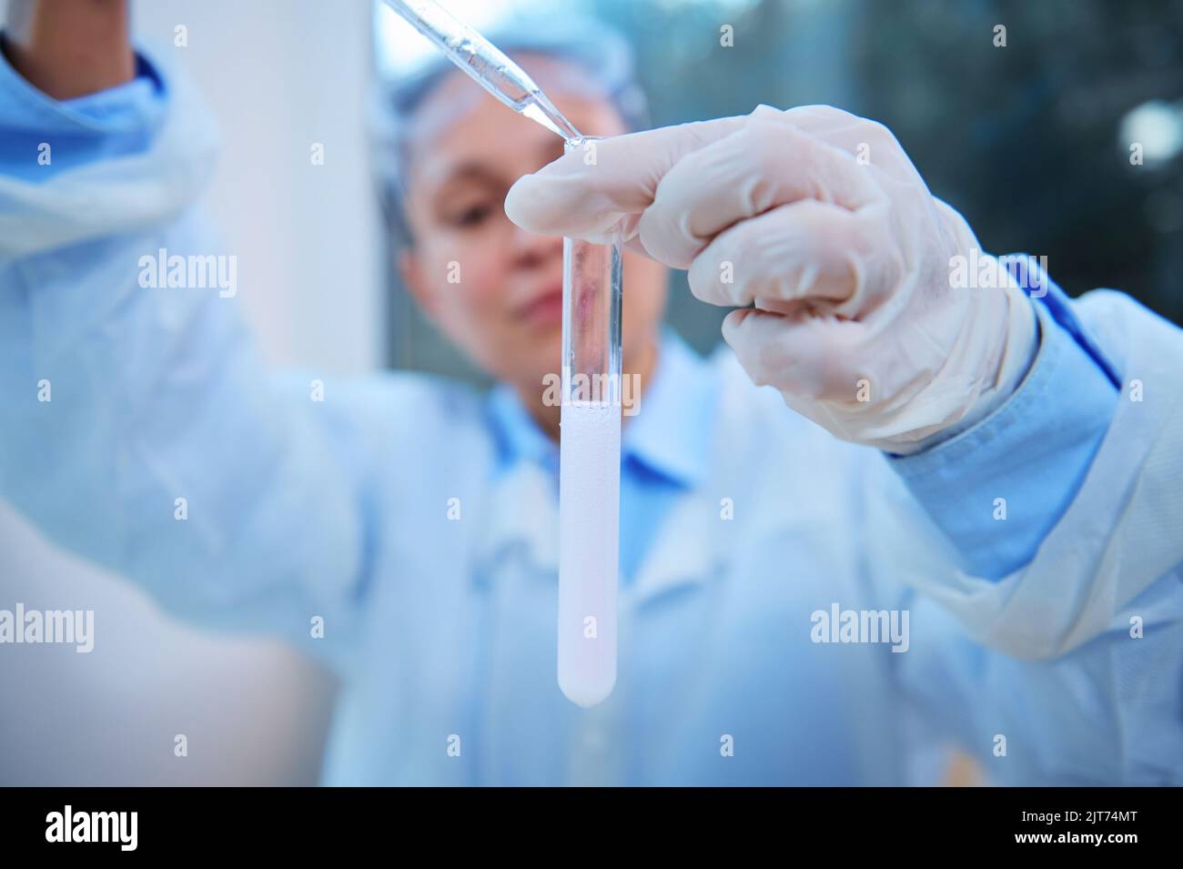 Hands of a lab assistant dripping a transparent liquid from a graduated ...