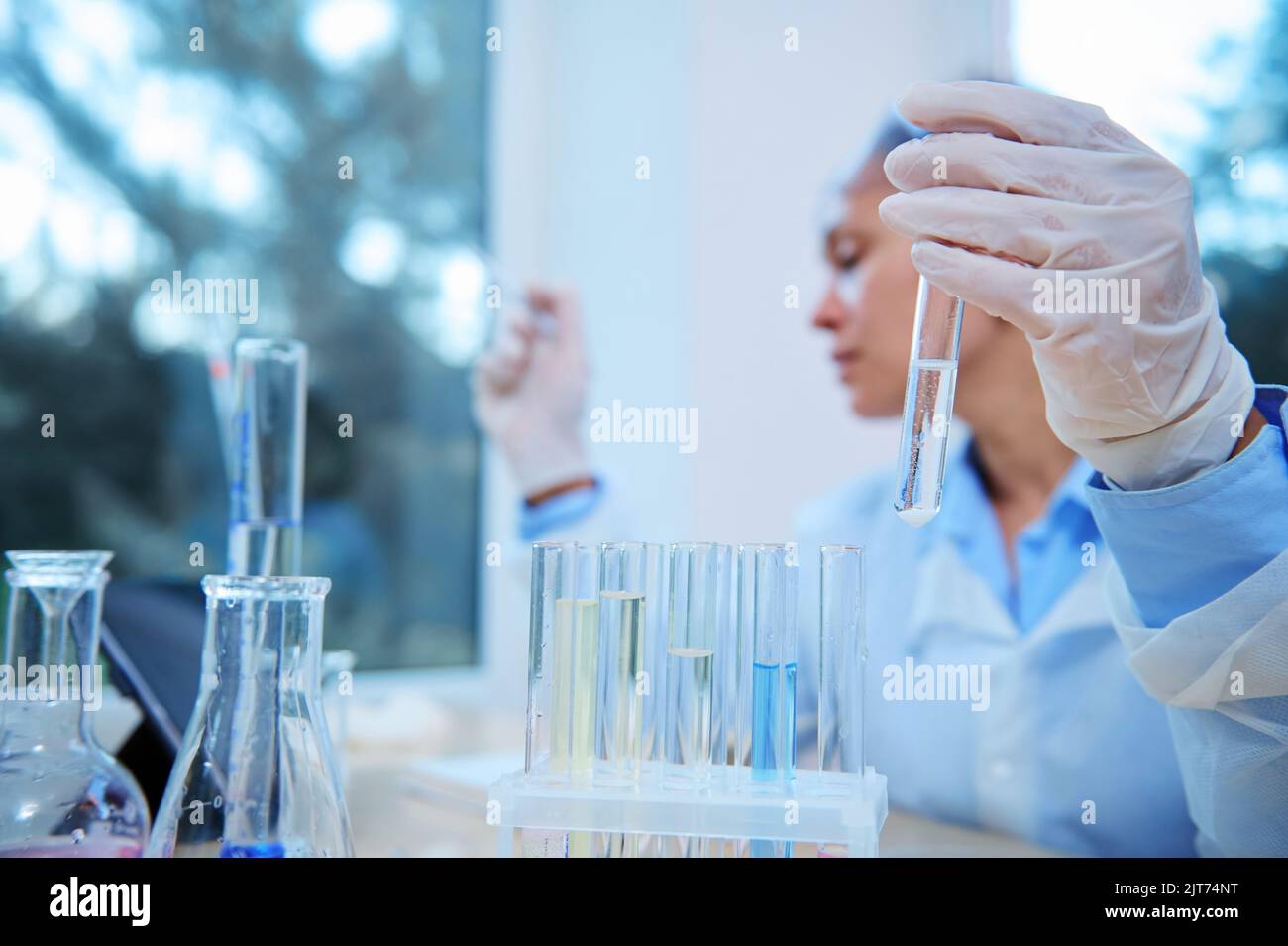 Test tube with chemical fluid in gloved hand of woman scientist chemist ...