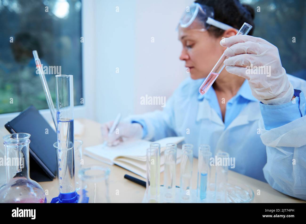 Test tube with solution, in the hand of scientist, writing down results ...