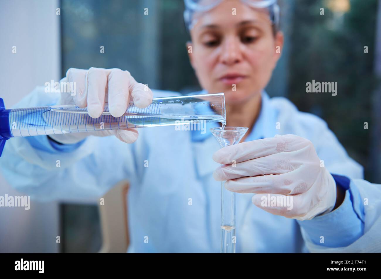Details: graduated cylinder in the hands of a blurred scientist pouring ...