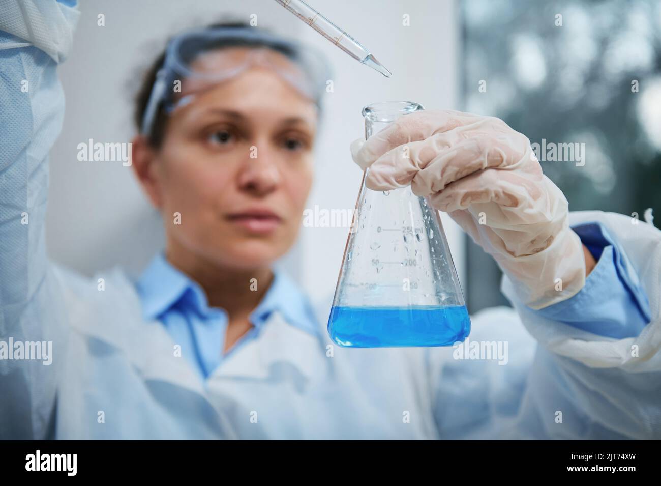 Focus on flat-bottomed flask and blurred charming woman scientist ...