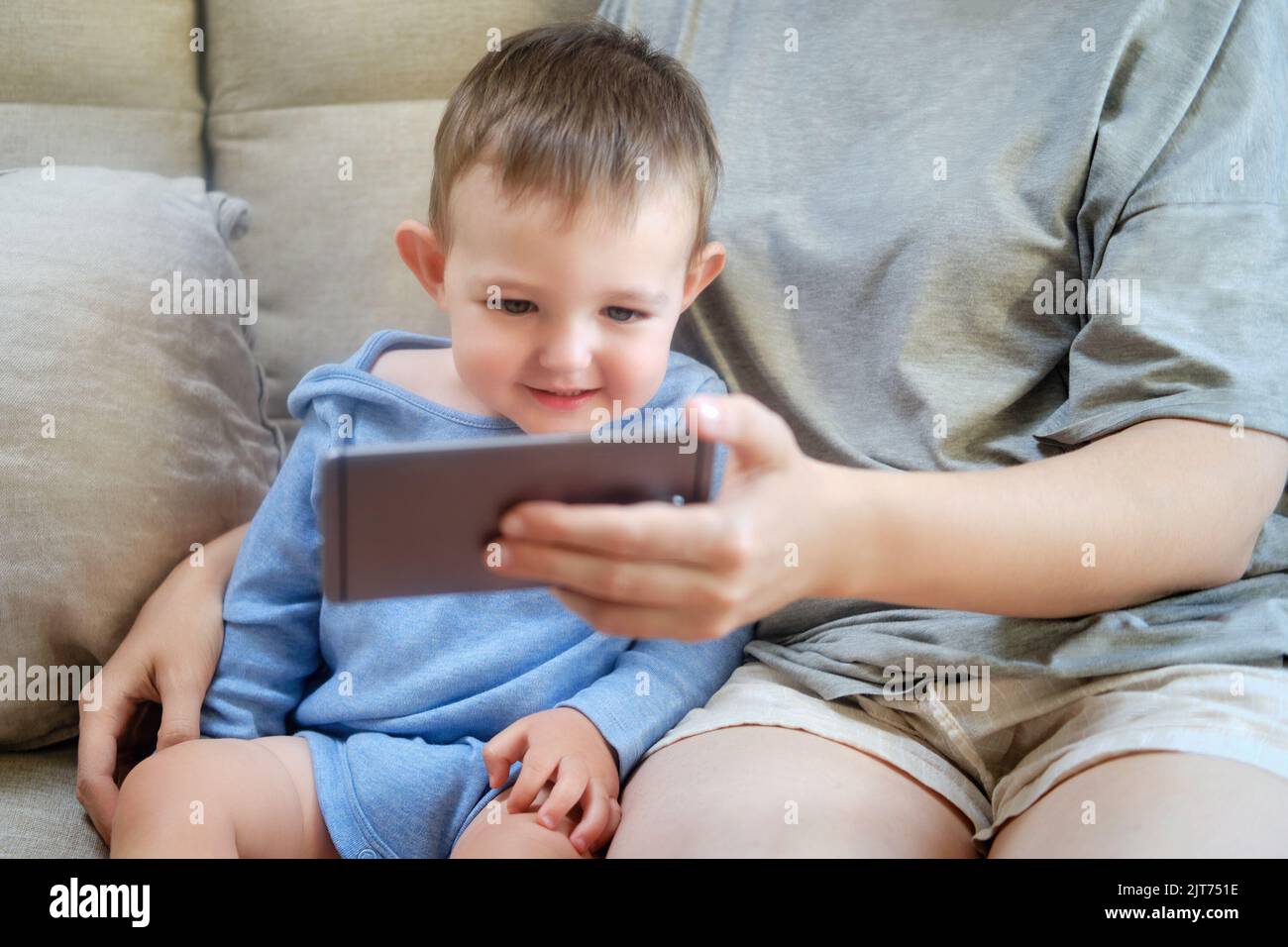Happy toddler boy sits with his mother and looks into the phone. Mom ...