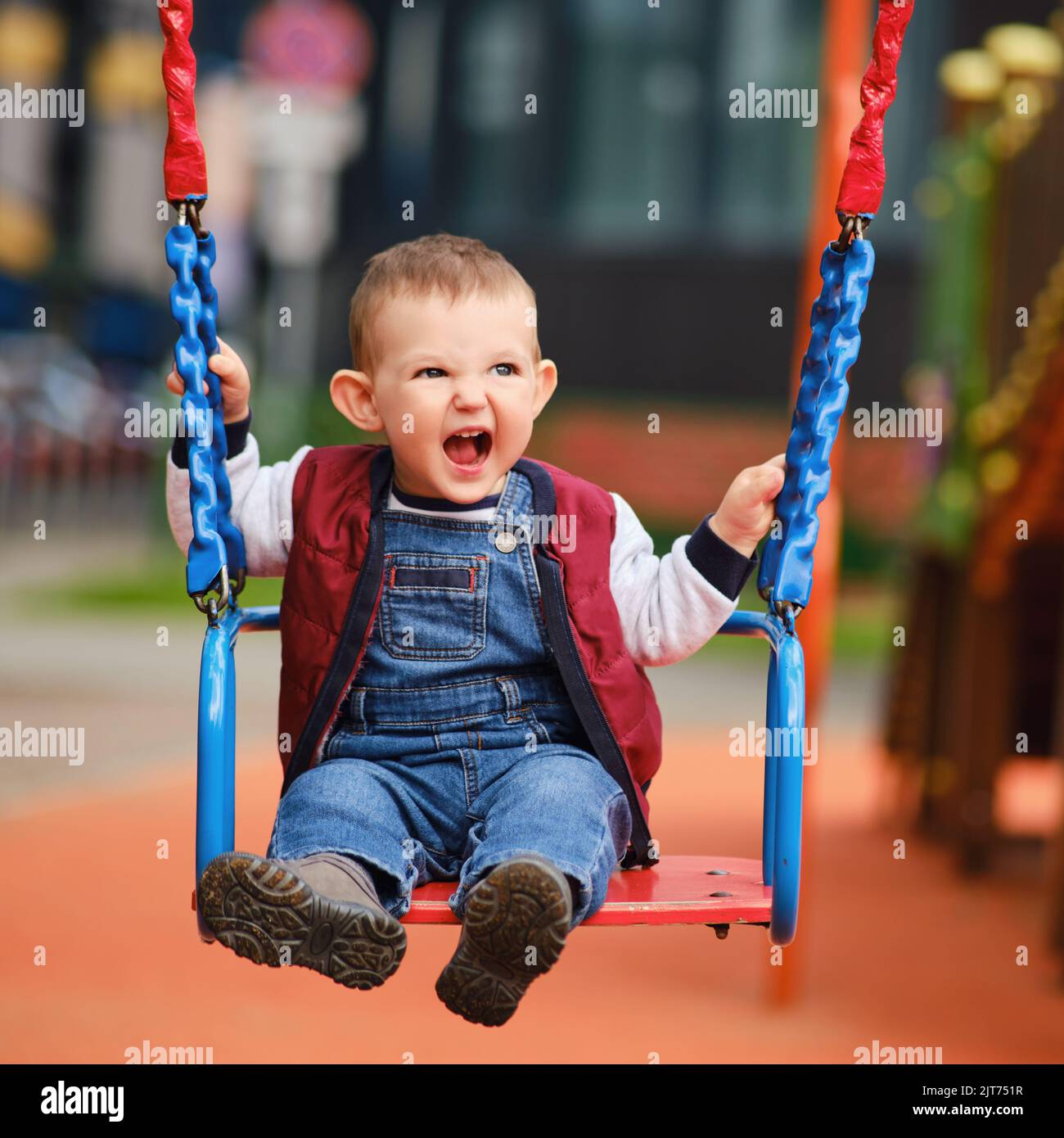 Screaming toddler baby boy rides on a swing. A frightened child swings ...