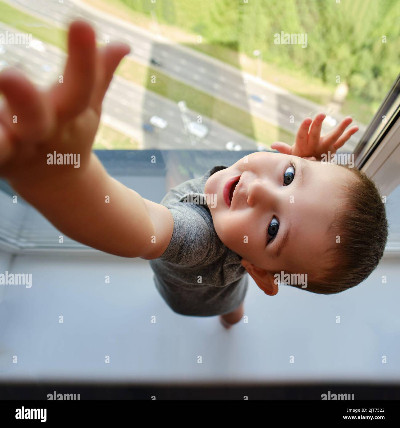Toddler baby is standing by the window on the windowsill. Child at the ...