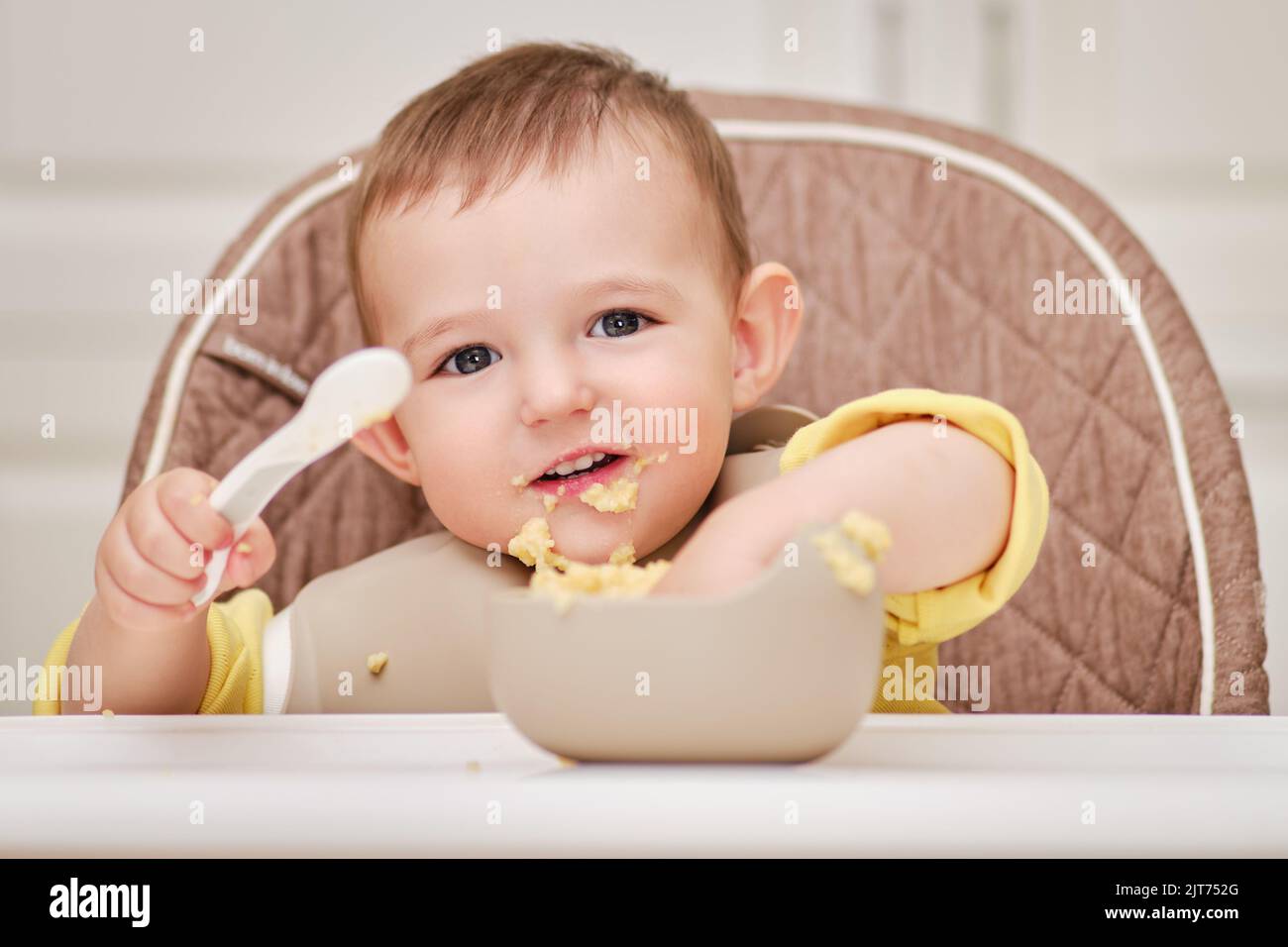 Happy toddler baby boy learns to eat porridge himself with a spoon ...