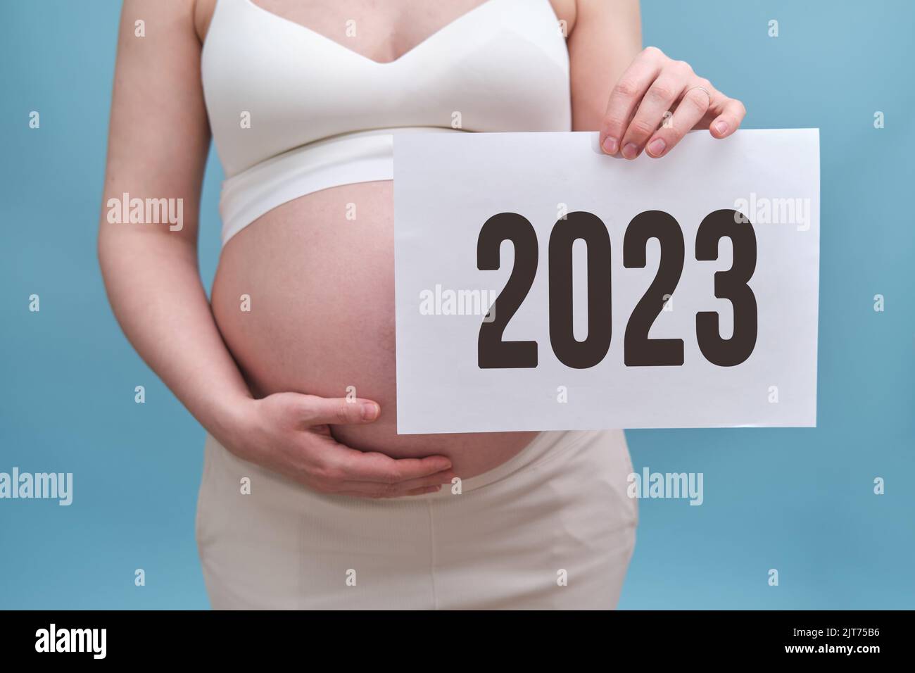 Pregnant woman holding a sheet of paper with the inscription 2023 year ...