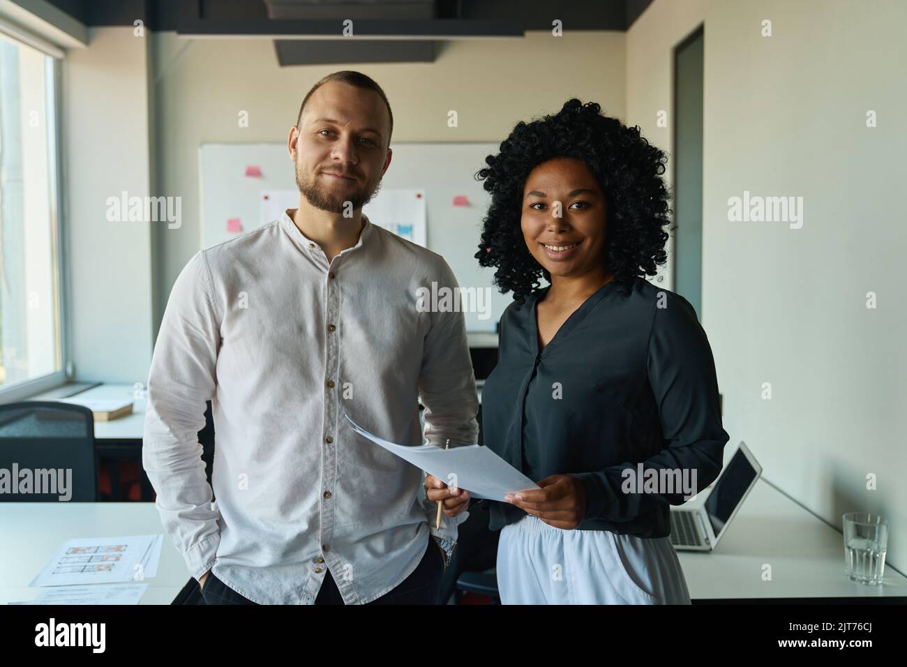 Smiling office workers stand side by side in the middle of the office ...