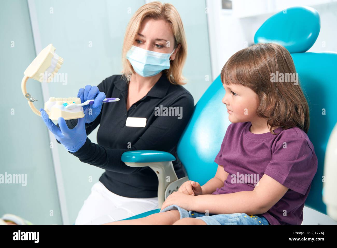 Dental hygienist teaching young female patient tooth-brushing technique ...