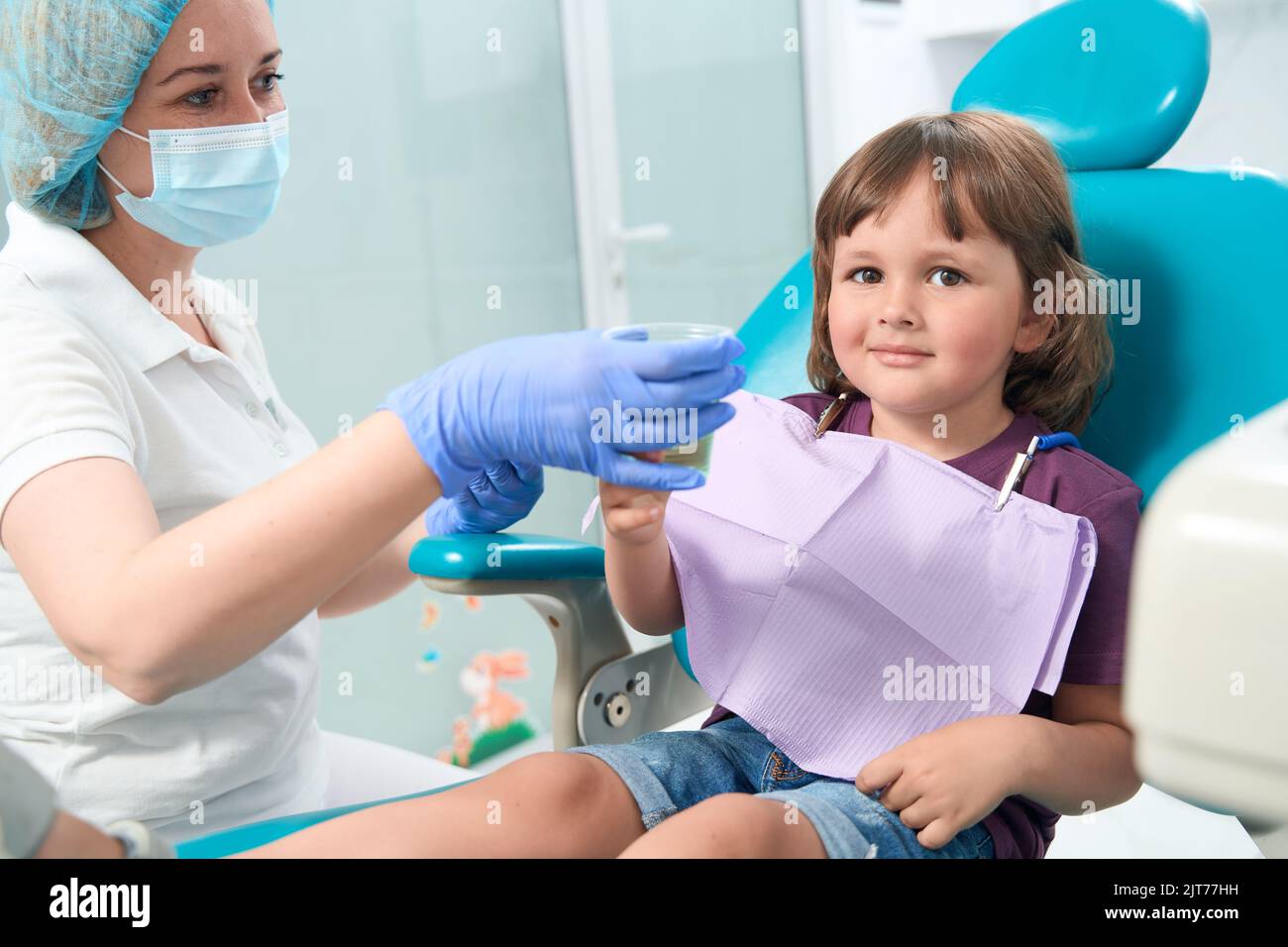 Pedodontist preparing little girl for rinsing mouth after procedure ...