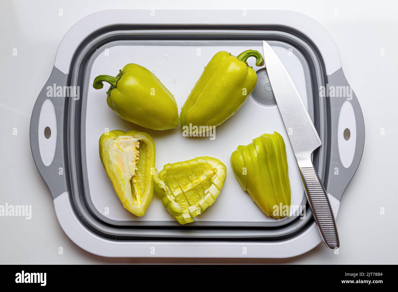 Green bell pepper, whole and chopped on a white cutting board with a ...