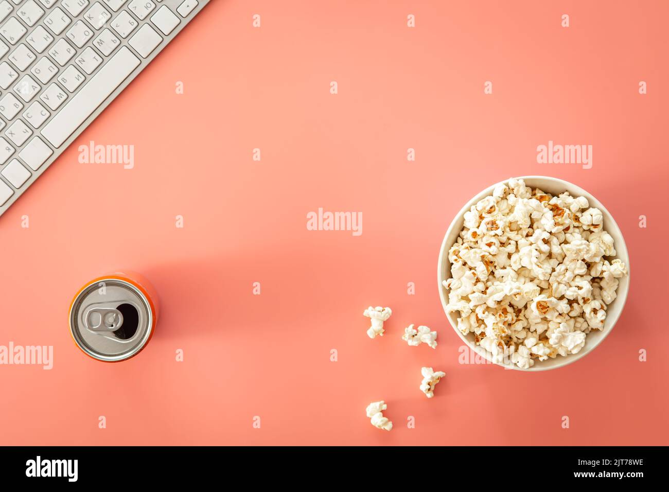 A bowl of popcorn, a keyboard and a can of drink on a pink background ...