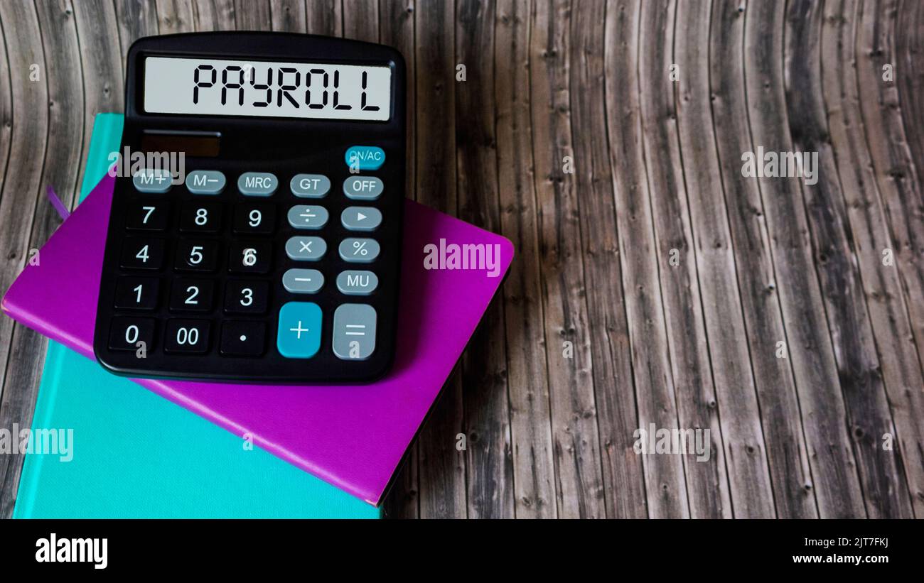 The word PAYROLL on a calculator display and a wooden table, time ...