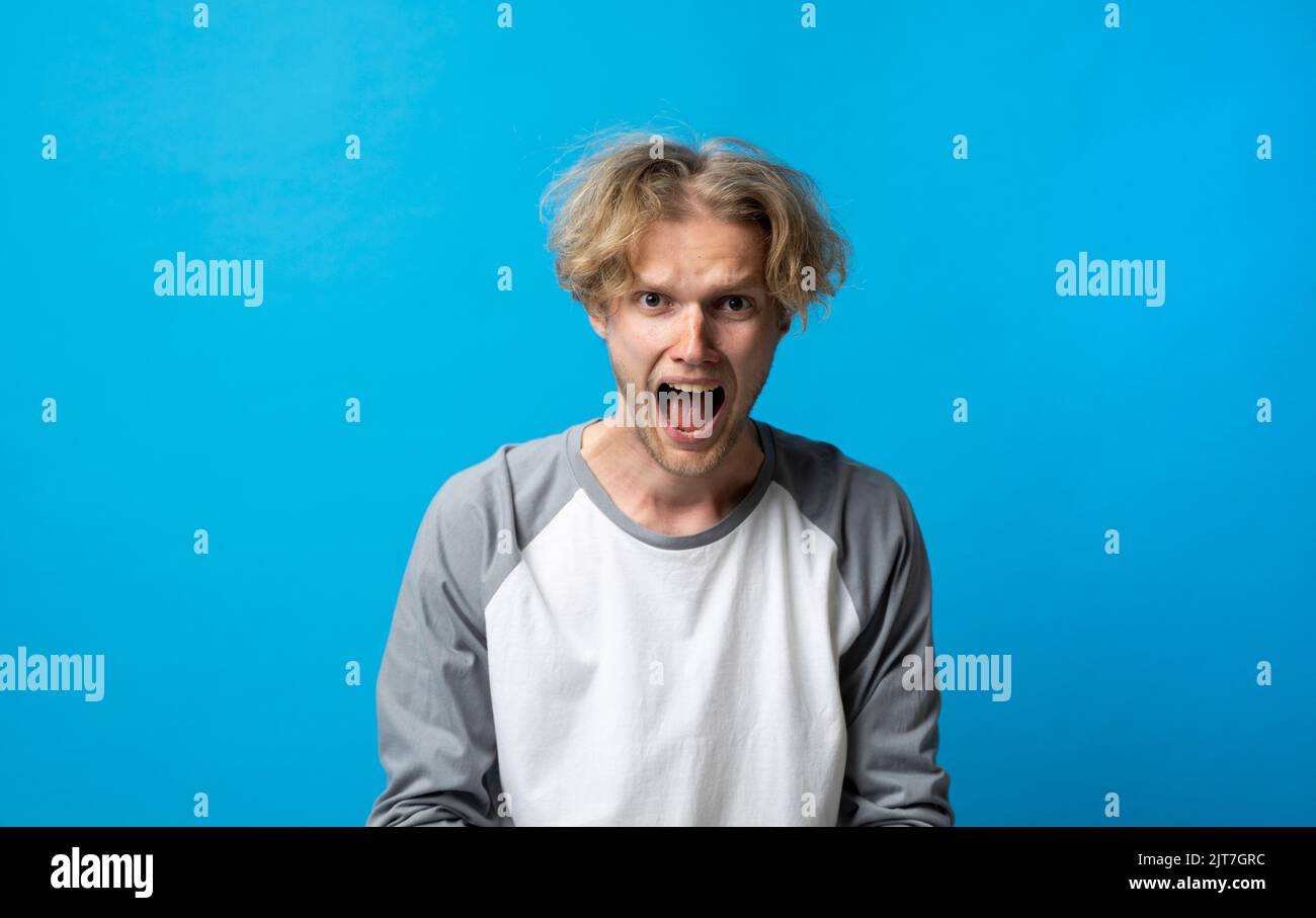 Angry, sad, aggressive young man screaming on a blue background ...