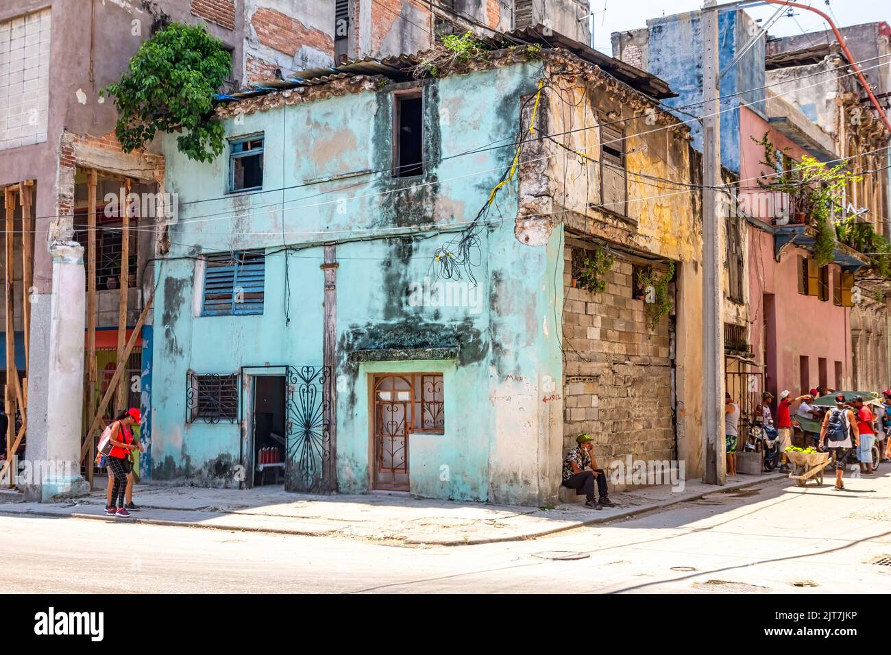 Cuban people are by a run-down building in a city corner. The image ...