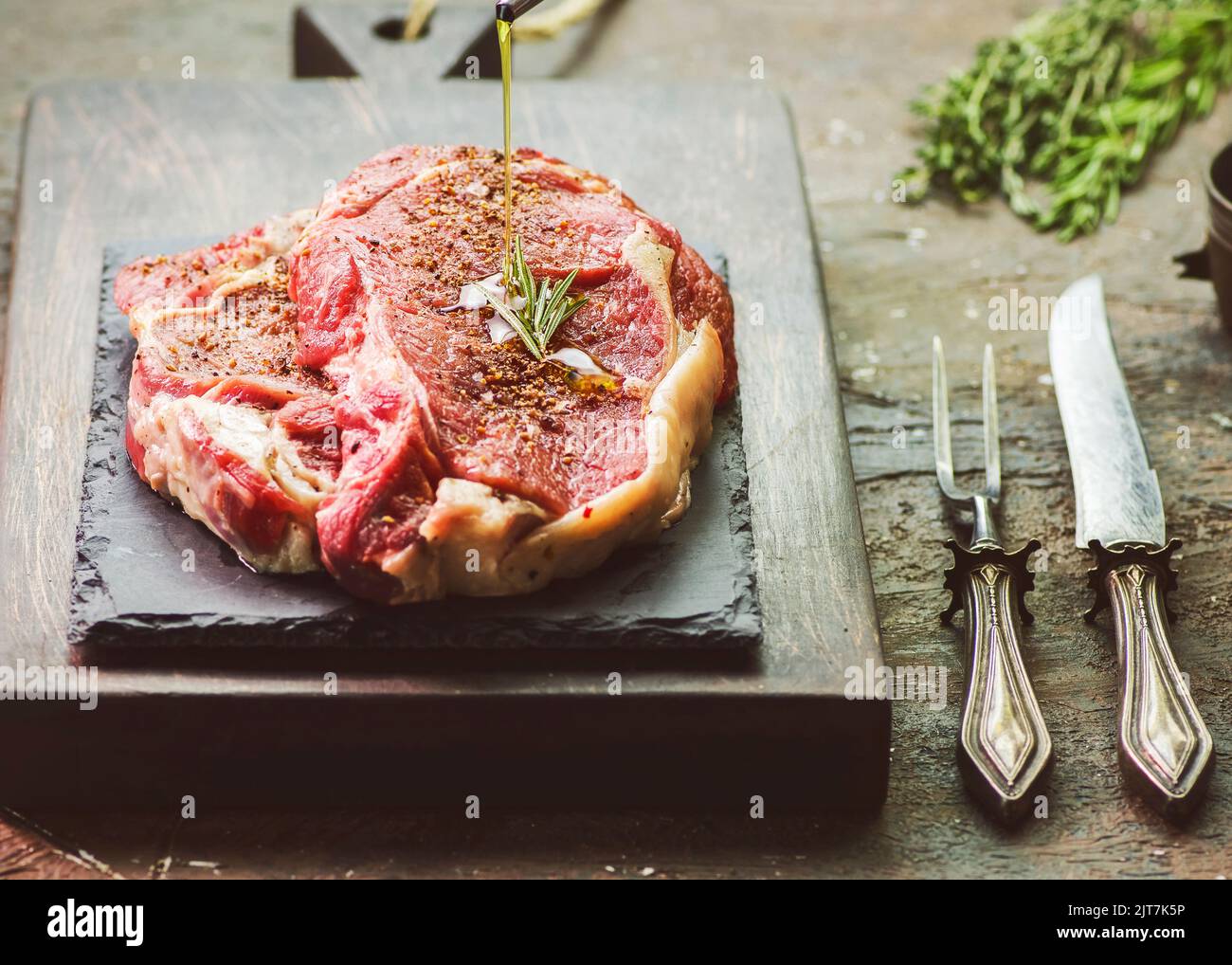 Pouring virgin olive oil on fresh raw beef steak with seasoning, butter ...