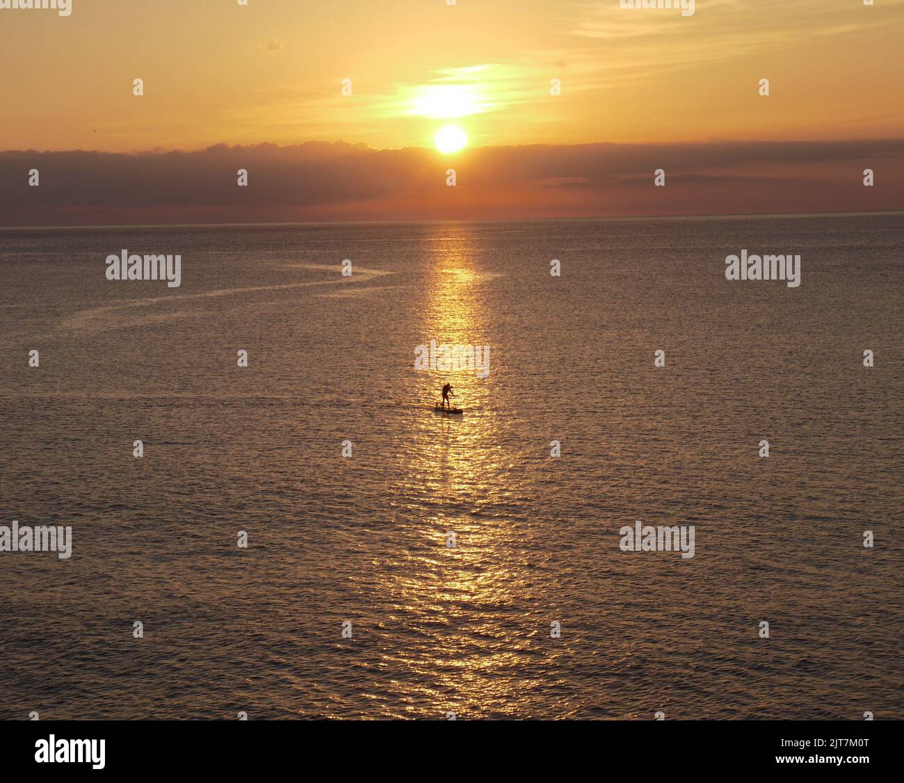 A paddleboarder crosses the sunset off Crackington Haven, Cornwall, UK ...