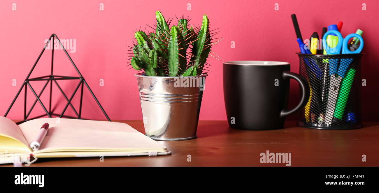 Green cactus, stationery and cup on table against pink wall Stock Photo ...