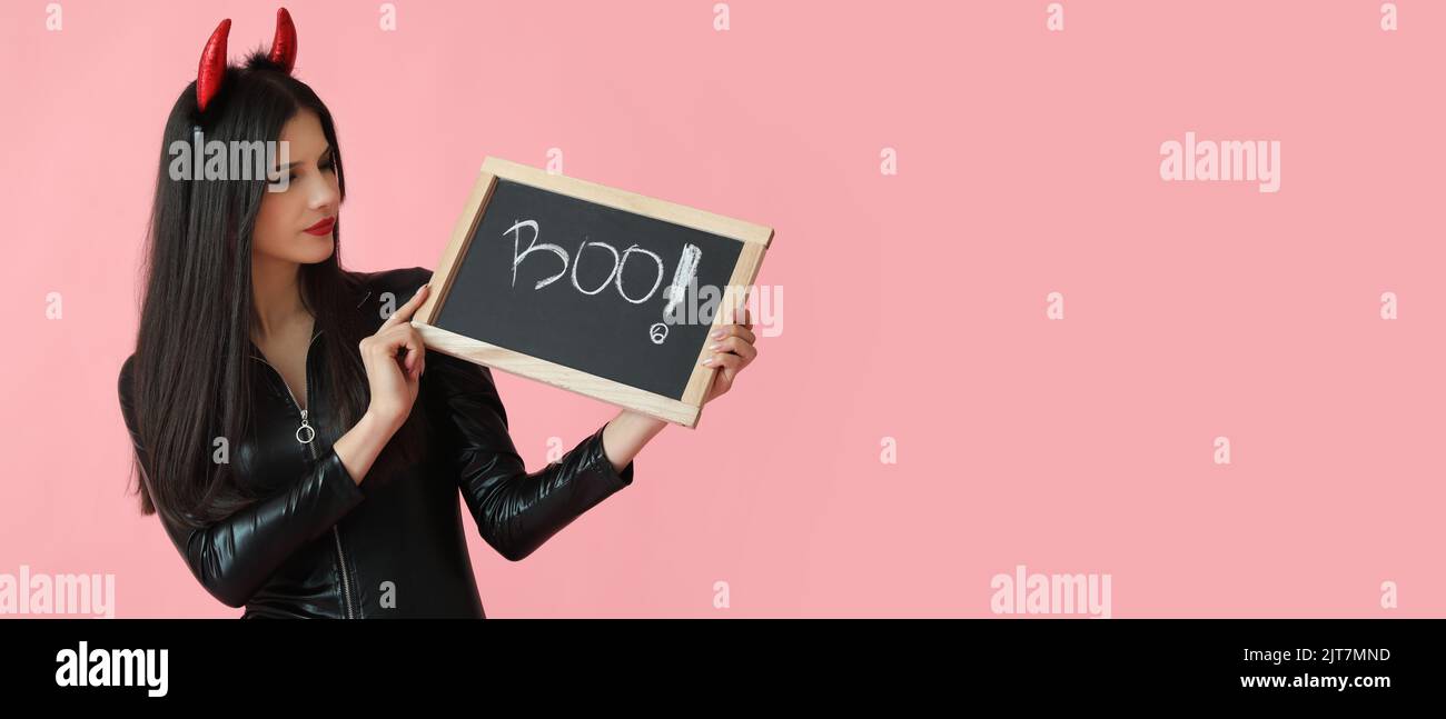 Beautiful young woman in Halloween costume holding chalkboard on pink ...