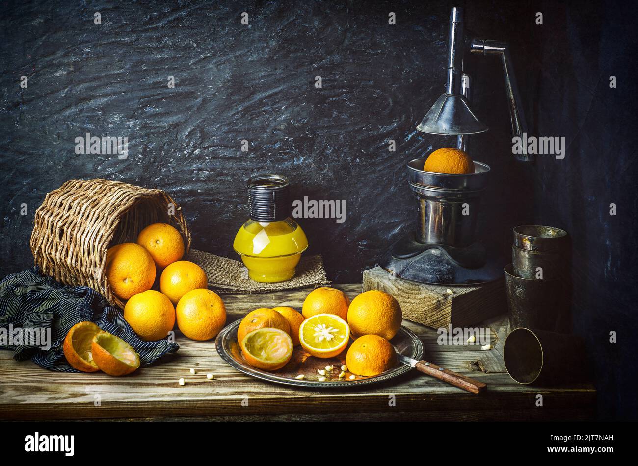 Classic still life with fresh oranges placed with old metal squeezer on rustic wooden background ...
