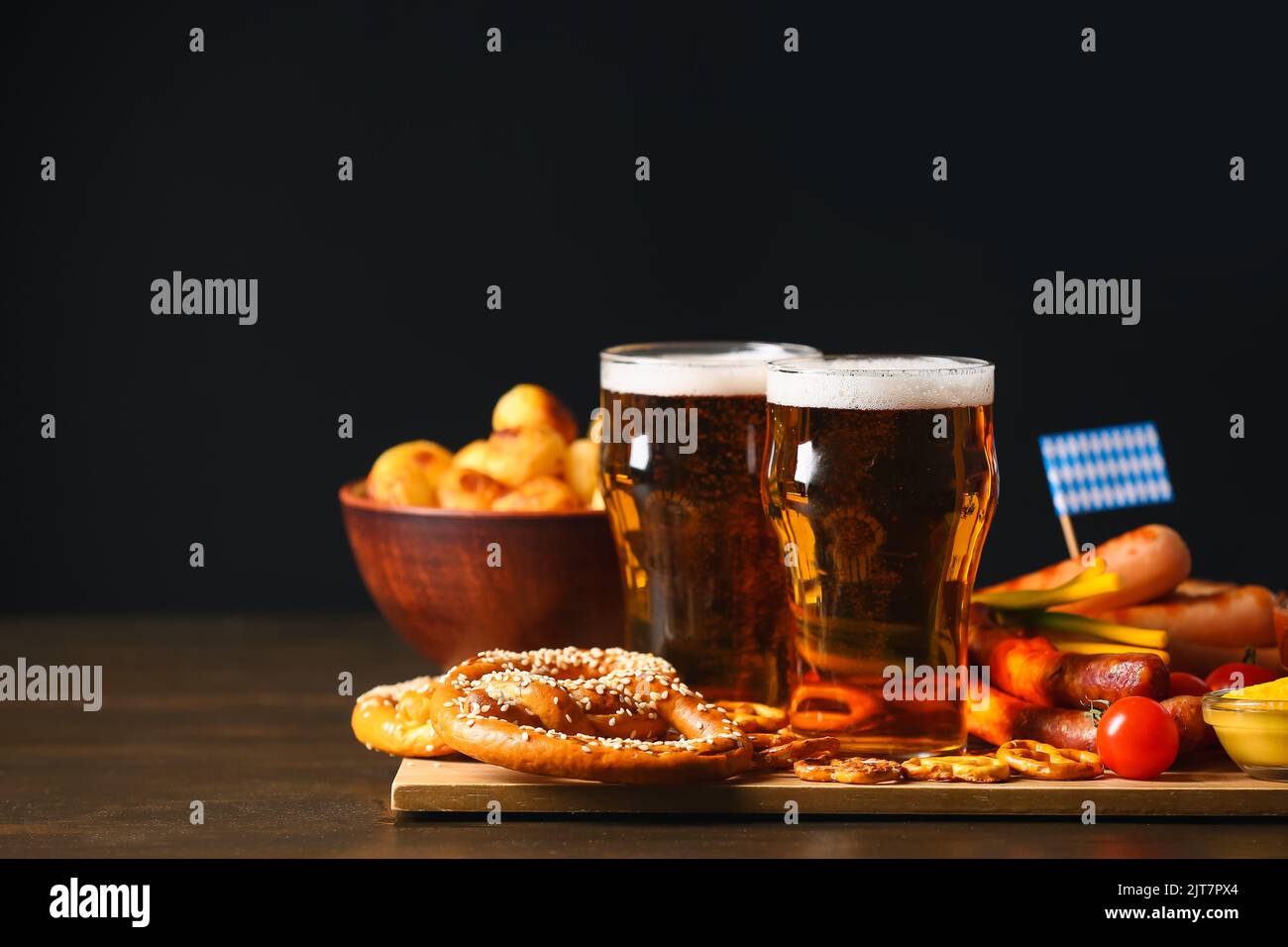 Board with glasses of beer, food and flags on table against dark ...