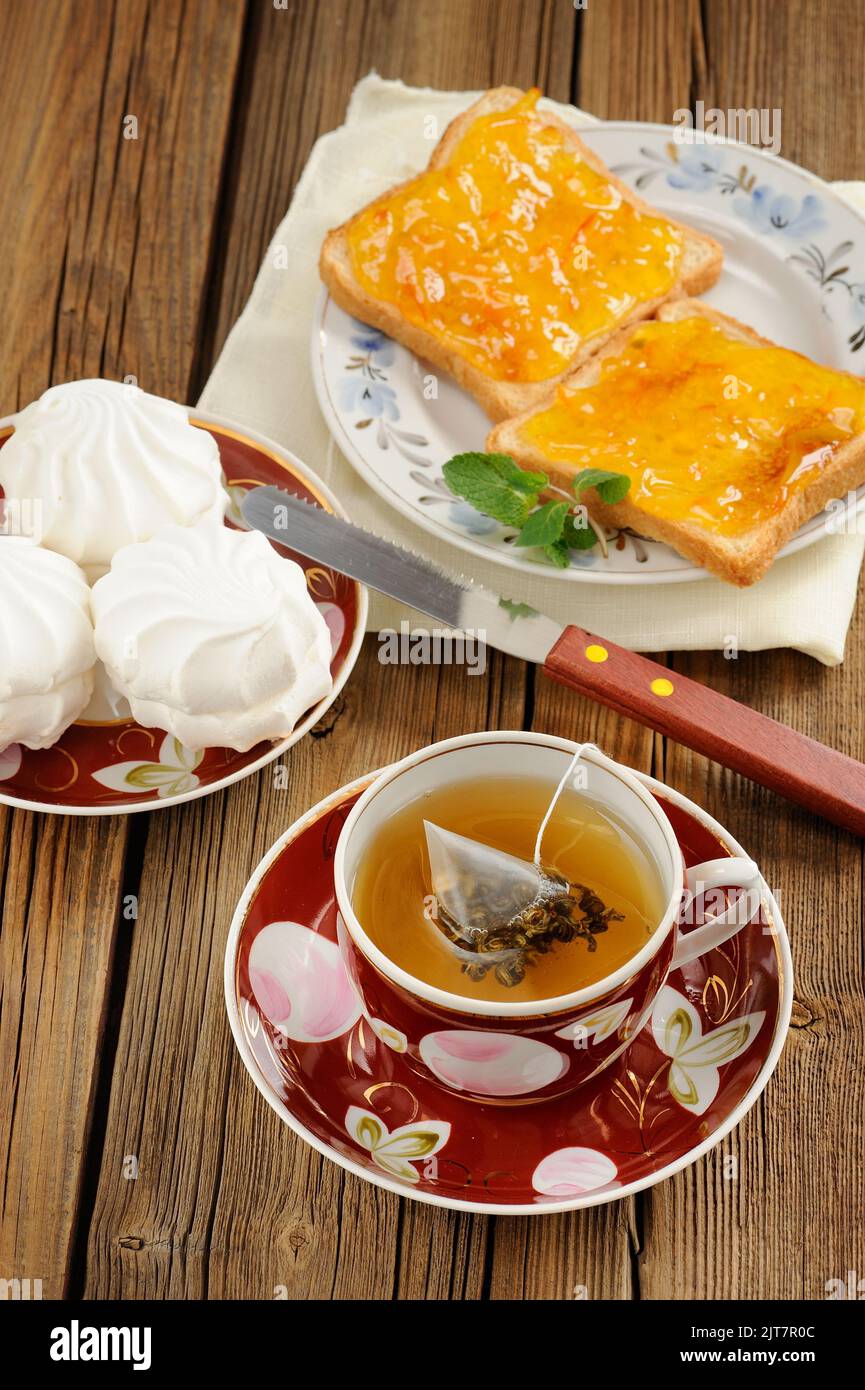 Green tea, zefir and toasts with orange marmalade on wooden background ...